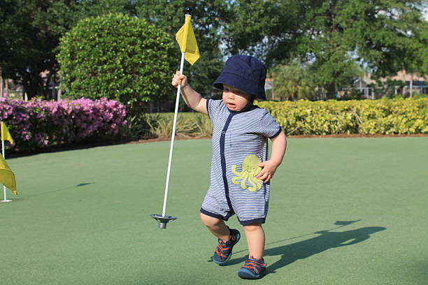 Baby walking across putting green holding yellow flag – Gianna House